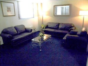 Sala de estar com carpete azul, dois sofás, uma mesa de centro e um abajur.