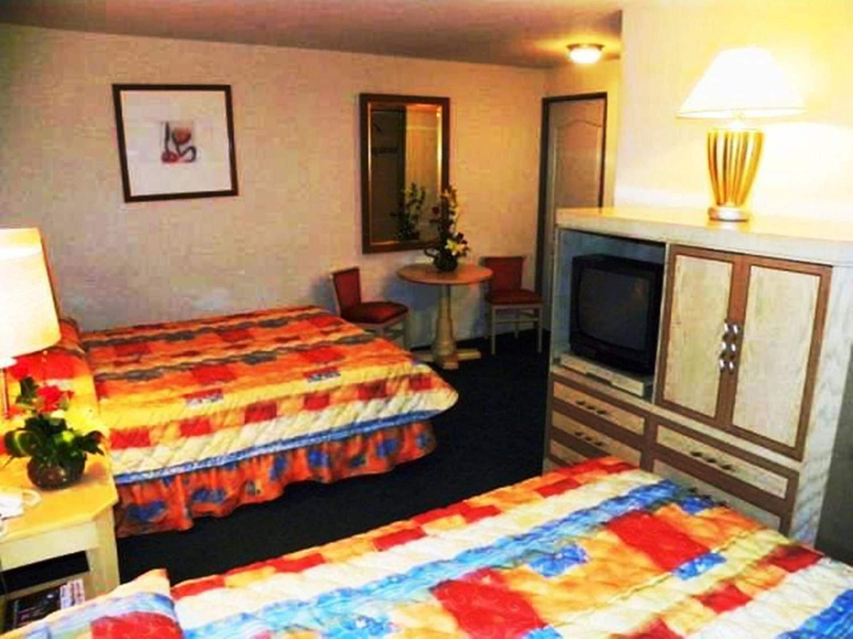Quarto de hotel com duas camas, televisão, escrivaninha e uma cadeira.