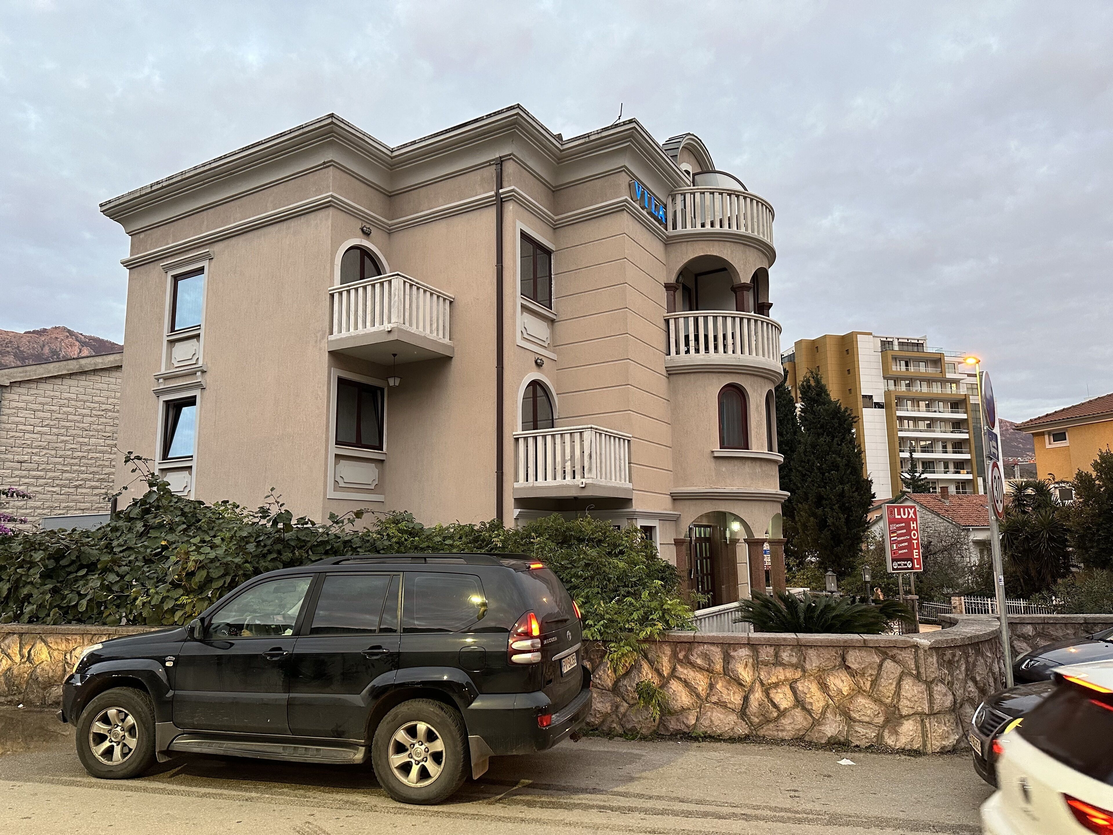 Um hotel com vários andares, varandas, uma parede de pedra e uma placa com o nome Lux Hotel.