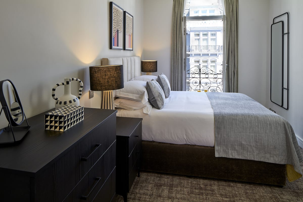 Quarto com cama, luminárias de cabeceira, cômoda, espelho e obras de arte na parede.