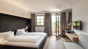 Quarto de hotel com uma cama grande, uma mesa com luminária, uma TV fixada na parede e uma porta deslizante para área externa.