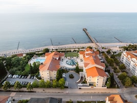 Vista aérea de um hotel com piscina, um pátio circular e um píer que se estende até o mar.