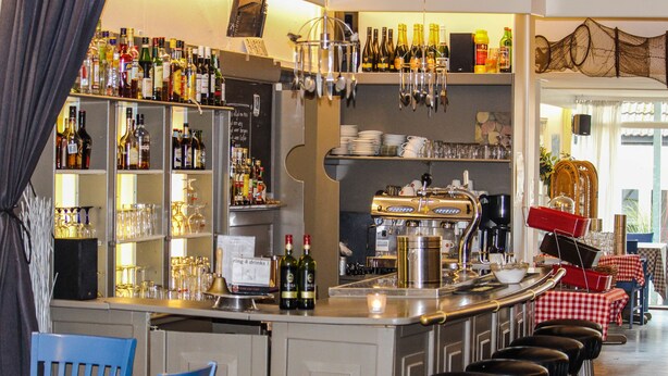 Uma área de bar com balcão, banquetas e prateleiras cheias de garrafas e copos.