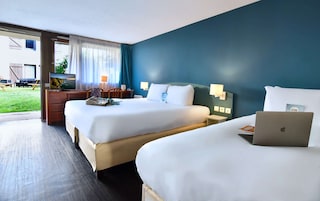 Quarto de hotel com duas camas, uma mesa, um laptop e vista para o exterior.