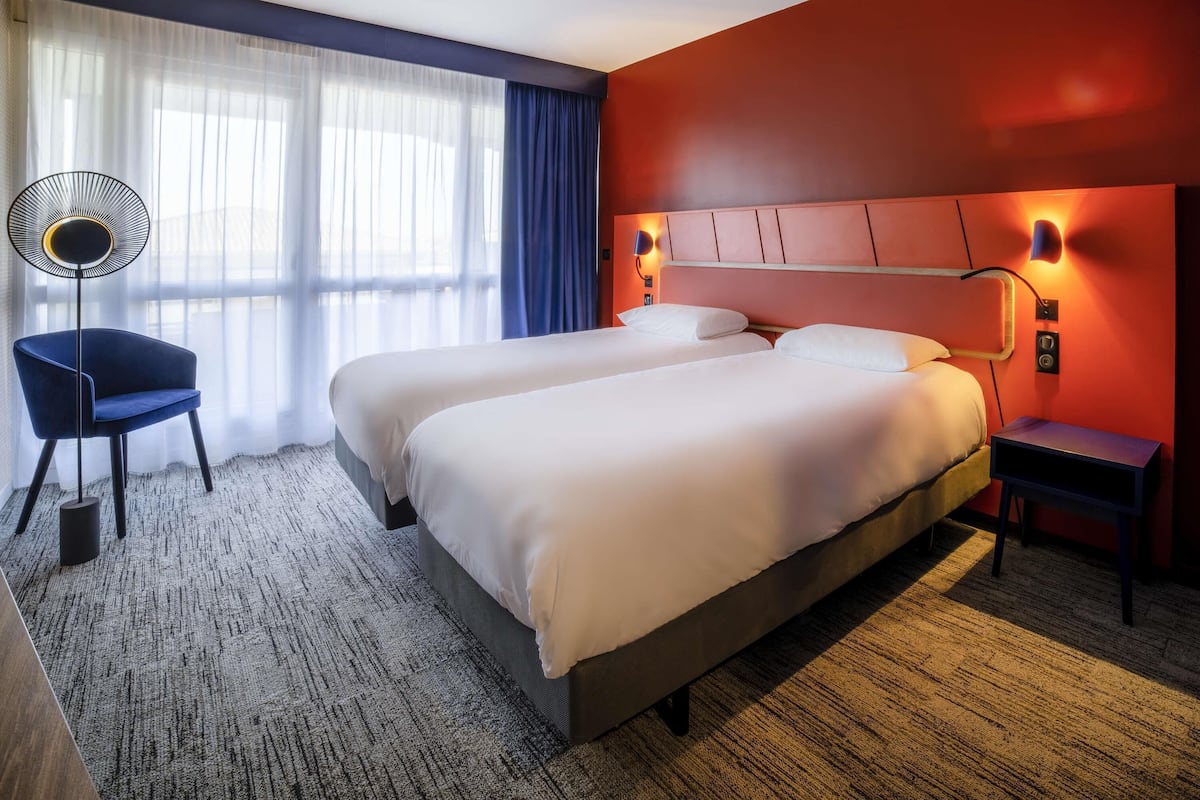 Quarto de hotel com uma cama grande, uma cadeira, uma escrivaninha e uma luminária.
