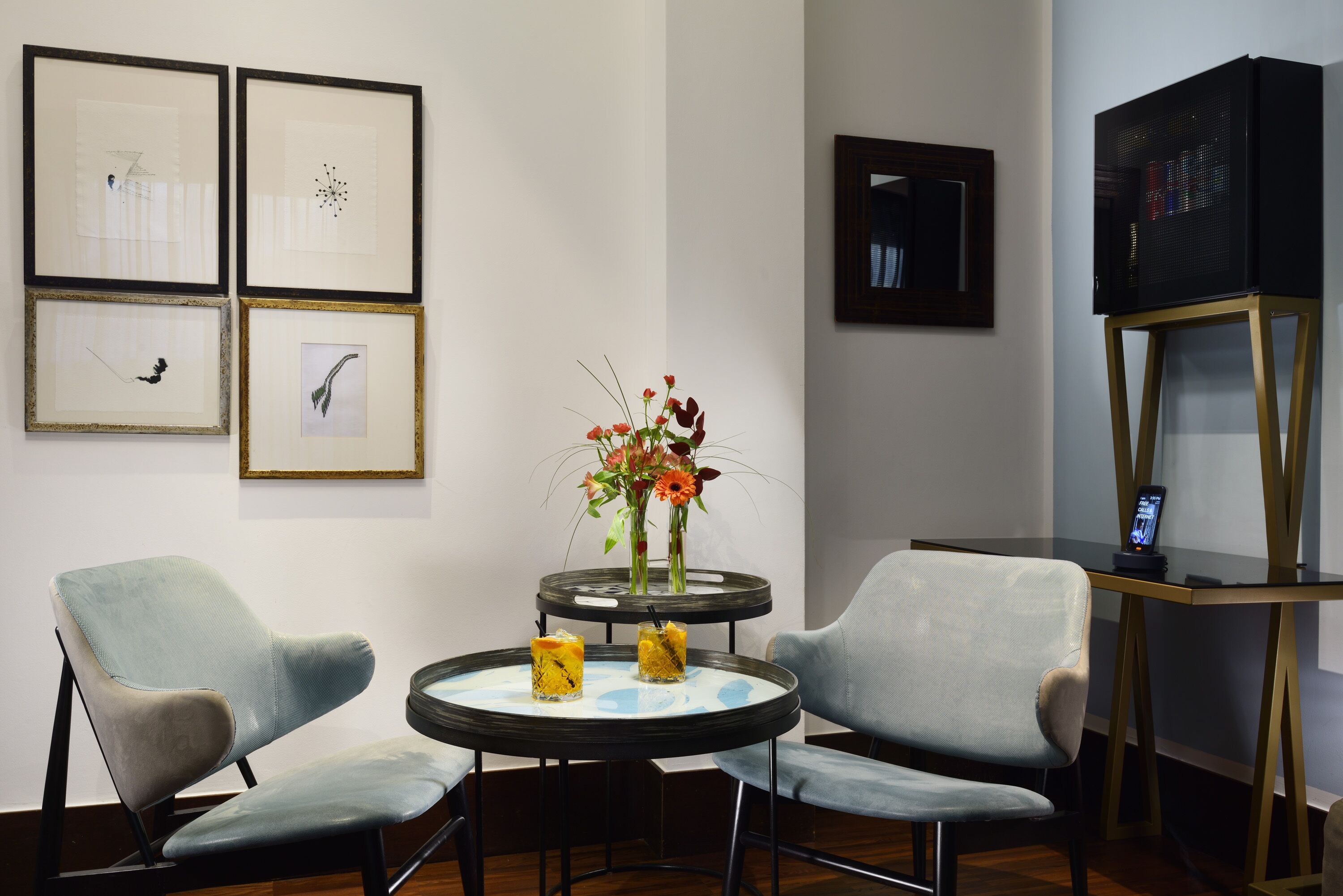 Um quarto com duas cadeiras azul-claras, uma pequena mesa redonda com um vaso de flores e um móvel de entretenimento preto.