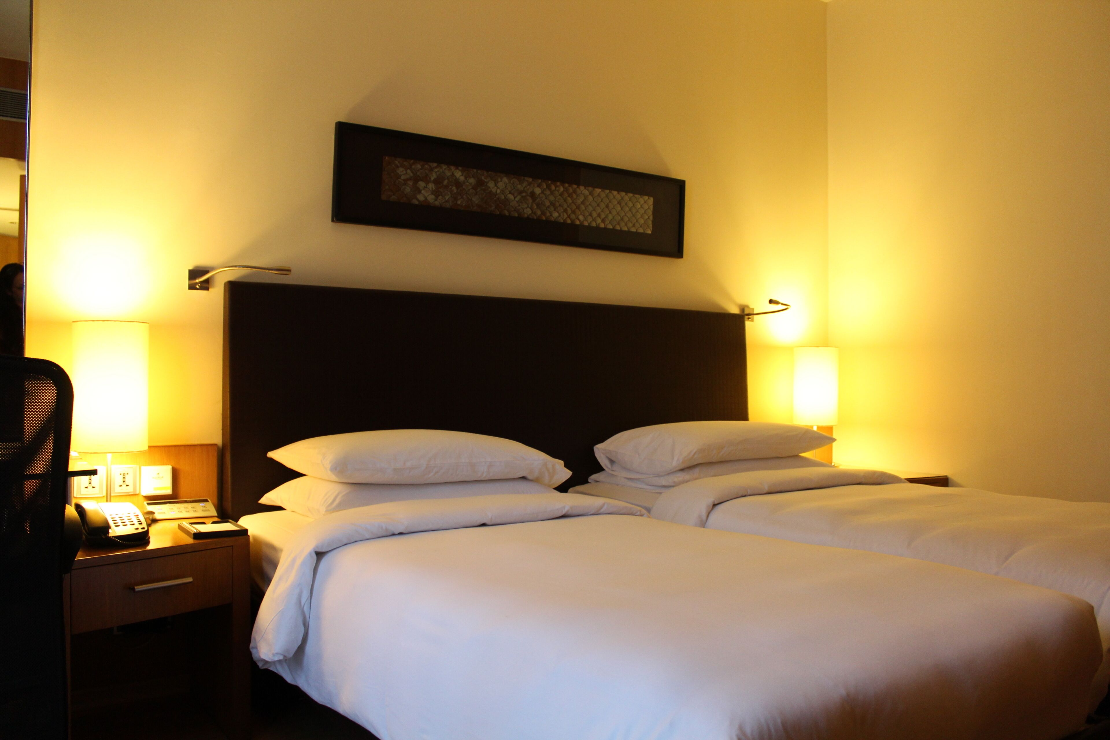 Quarto de hotel com duas camas, uma escrivaninha com abajur e um telefone.