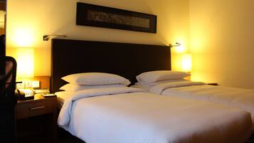 Quarto de hotel com duas camas, uma escrivaninha com abajur e um telefone.