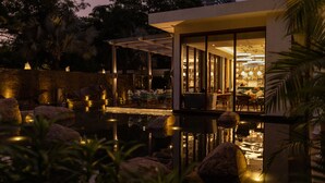 Uma área moderna de piscina ao ar livre com assentos e bar, cercada por pedras e palmeiras.