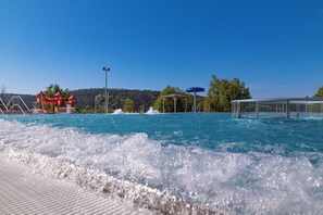 Uma piscina com água salpicando, um guarda-sol e vista para árvores e colinas ao fundo.