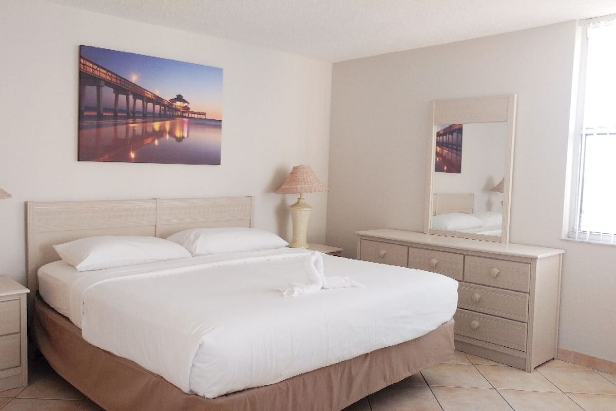 Quarto com cama, mesas de cabeceira, cômoda, espelho e um quadro na parede.