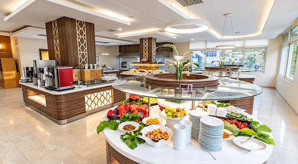 Espaço de café da manhã moderno em hotel, com buffet variado, comidas diversas e estação de café.
