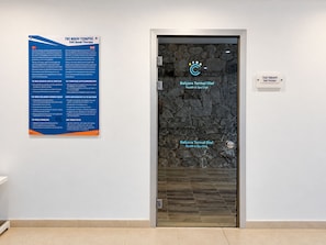 Uma porta com um aviso indicando uma área de terapia com sal, parede de pedra e piso de azulejos.