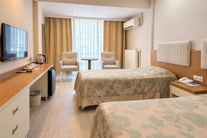 Quarto de hotel com duas camas, uma escrivaninha com televisão, uma cafeteira e uma pequena mesa.