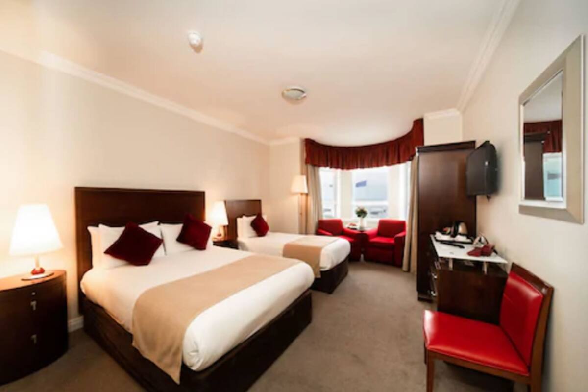 Quarto de hotel com duas camas, uma escrivaninha, uma cadeira e uma televisão.