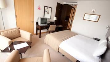 Quarto de hotel com cama, escrivaninha com computador, cadeira, sofá e abajur.