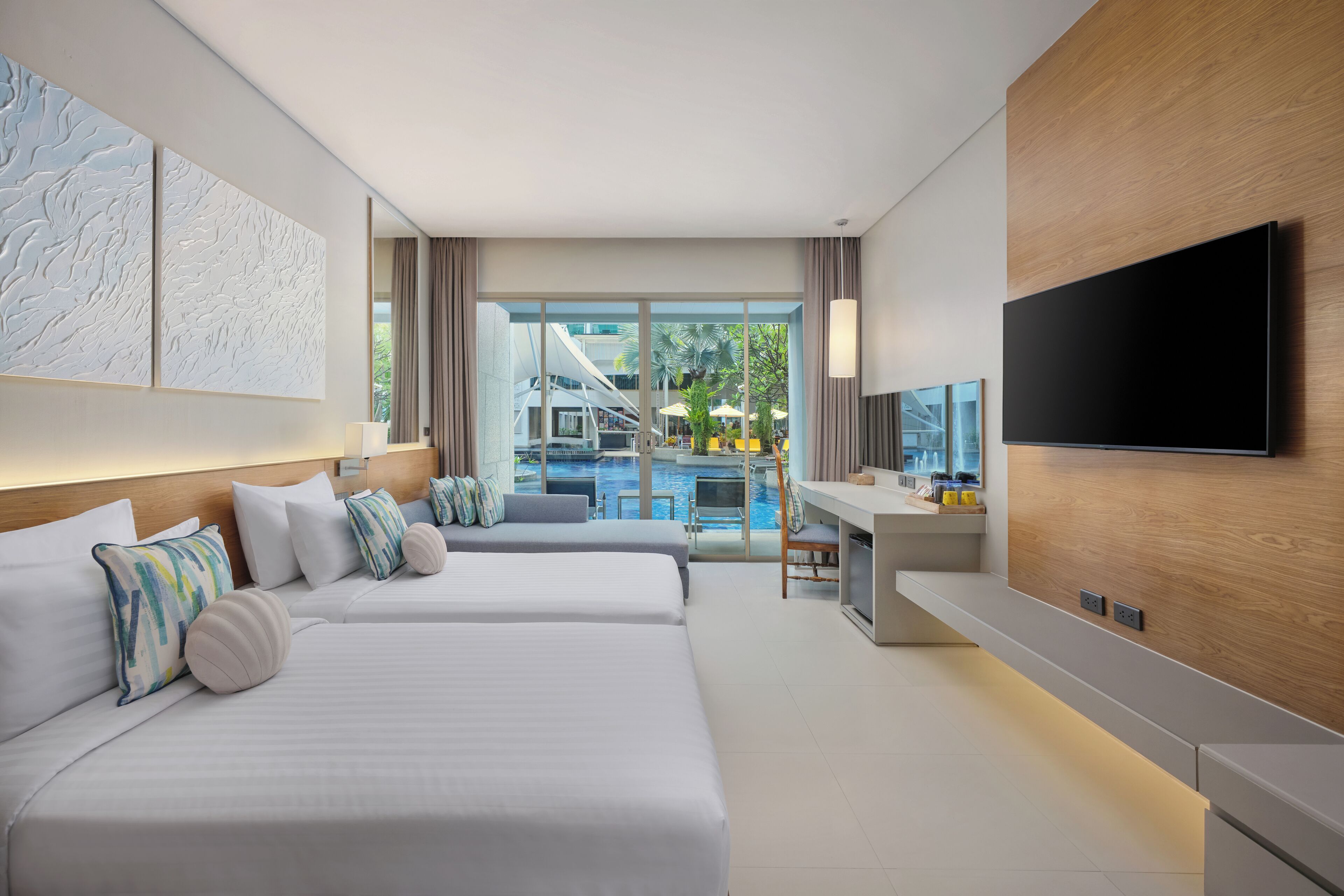 Quarto de hotel moderno com duas camas, uma escrivaninha, televisão de tela plana e vista para a piscina e área externa.