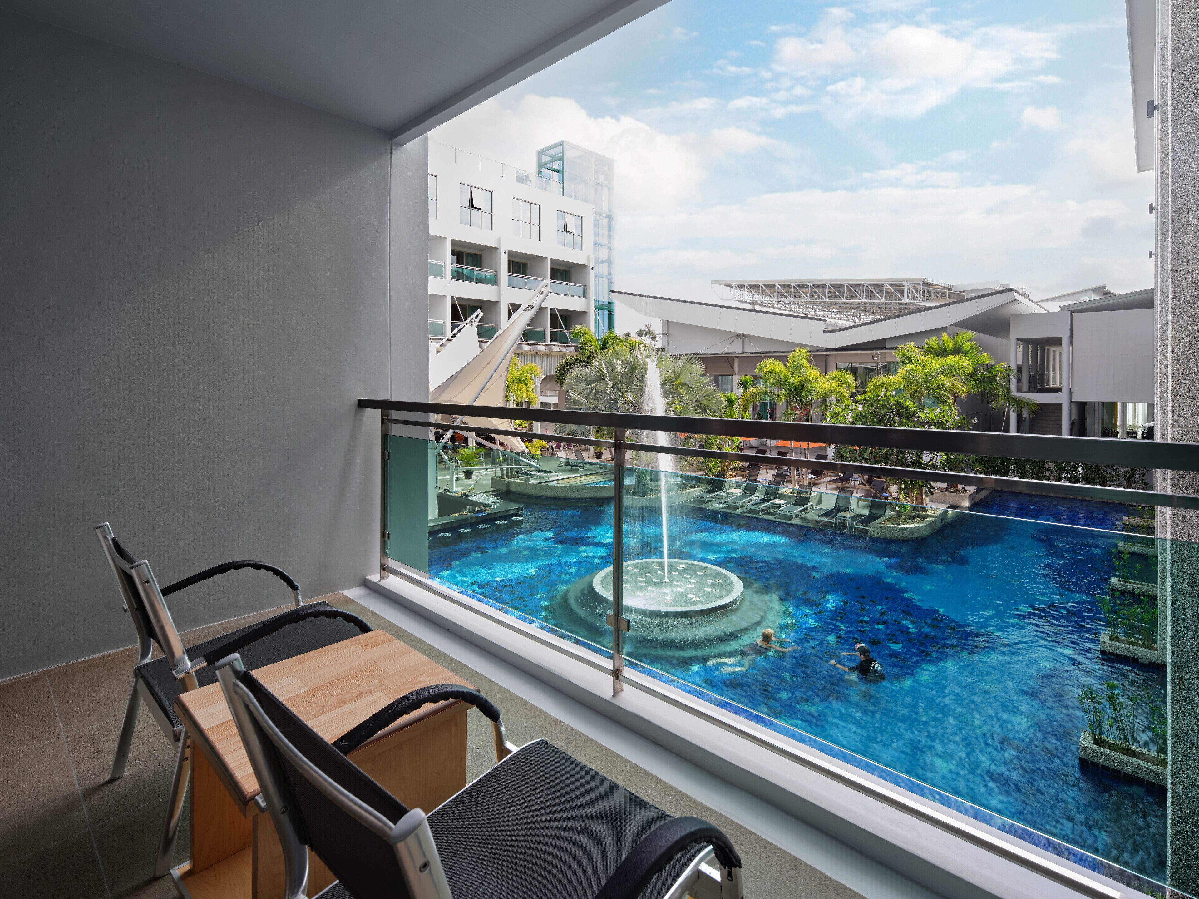 Uma varanda com vista para uma piscina, cadeiras de descanso e um edifício moderno ao fundo.
