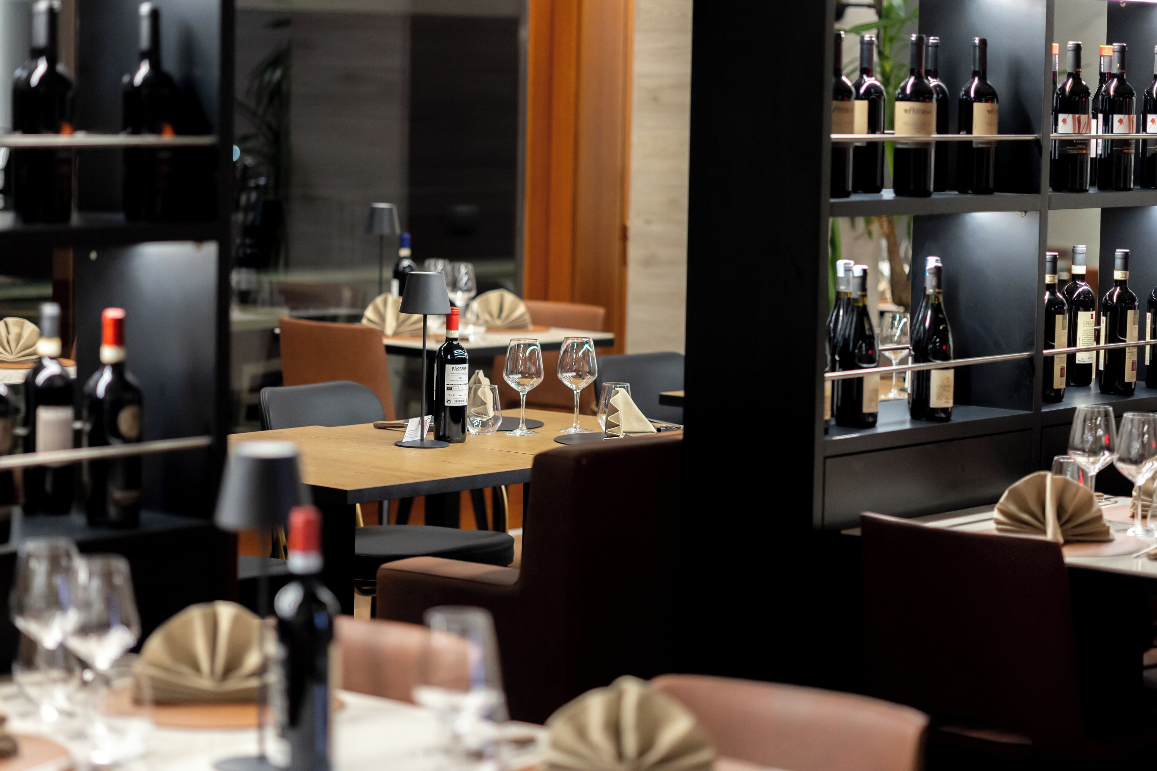 Interior de restaurante com várias mesas, cadeiras e prateleiras cheias de garrafas de vinho.
