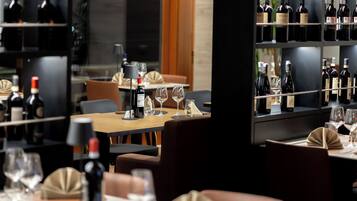 Interior de restaurante com várias mesas, cadeiras e prateleiras cheias de garrafas de vinho.