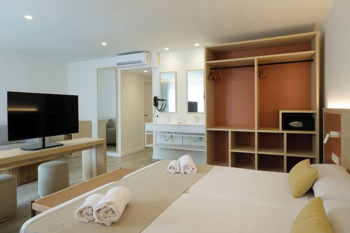 Quarto de hotel com cama, televisão, escrivaninha, guarda-roupa e banheiro.