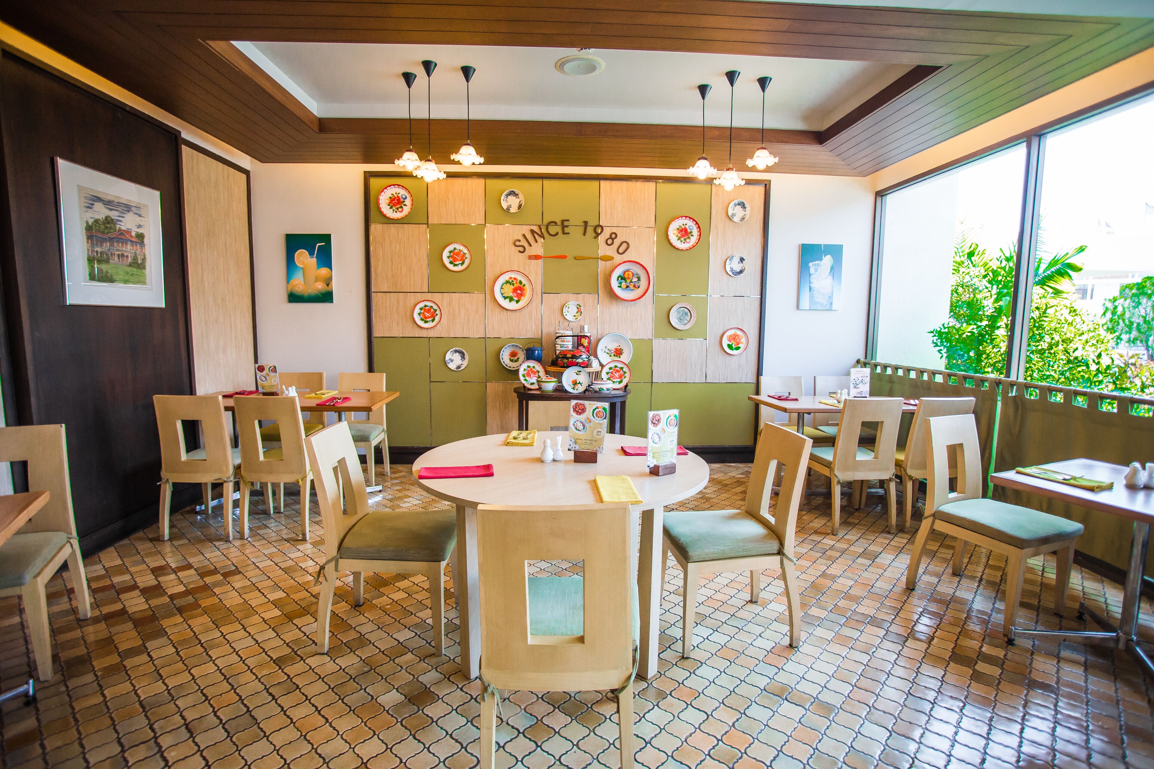 Um restaurante com chão de azulejos, cadeiras de madeira, uma mesa redonda e uma parede decorada com pratos e um letreiro que diz "SINCE 1980".