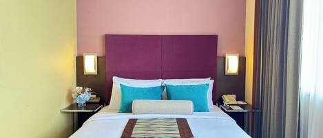 Quarto de hotel com uma cama grande, cabeceira, duas mesas de cabeceira com luminárias e uma janela com cortinas.