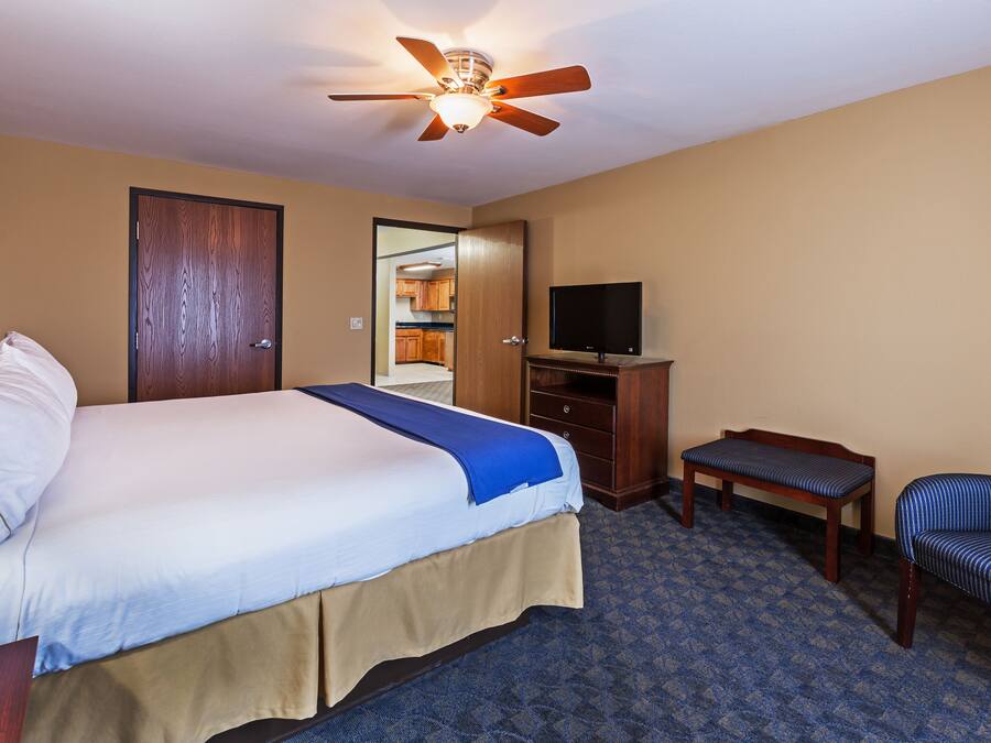 Quarto de hotel com cama, escrivaninha, cadeira, televisão e ventoinha no teto.