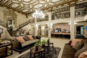 Um hall amplo com uma escadaria imponente, uma mesa de recepção e várias áreas de estar.