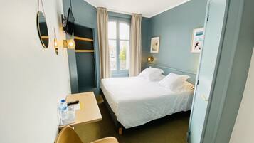 Quarto de hotel com cama, escrivaninha, cadeira, televisão e janela com cortinas.