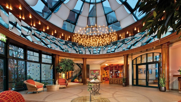 Um hall amplo com teto alto, janelas grandes e um lustre central.