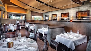 Restaurante com mesas redondas, cabines e teto alto com vigas aparentes.