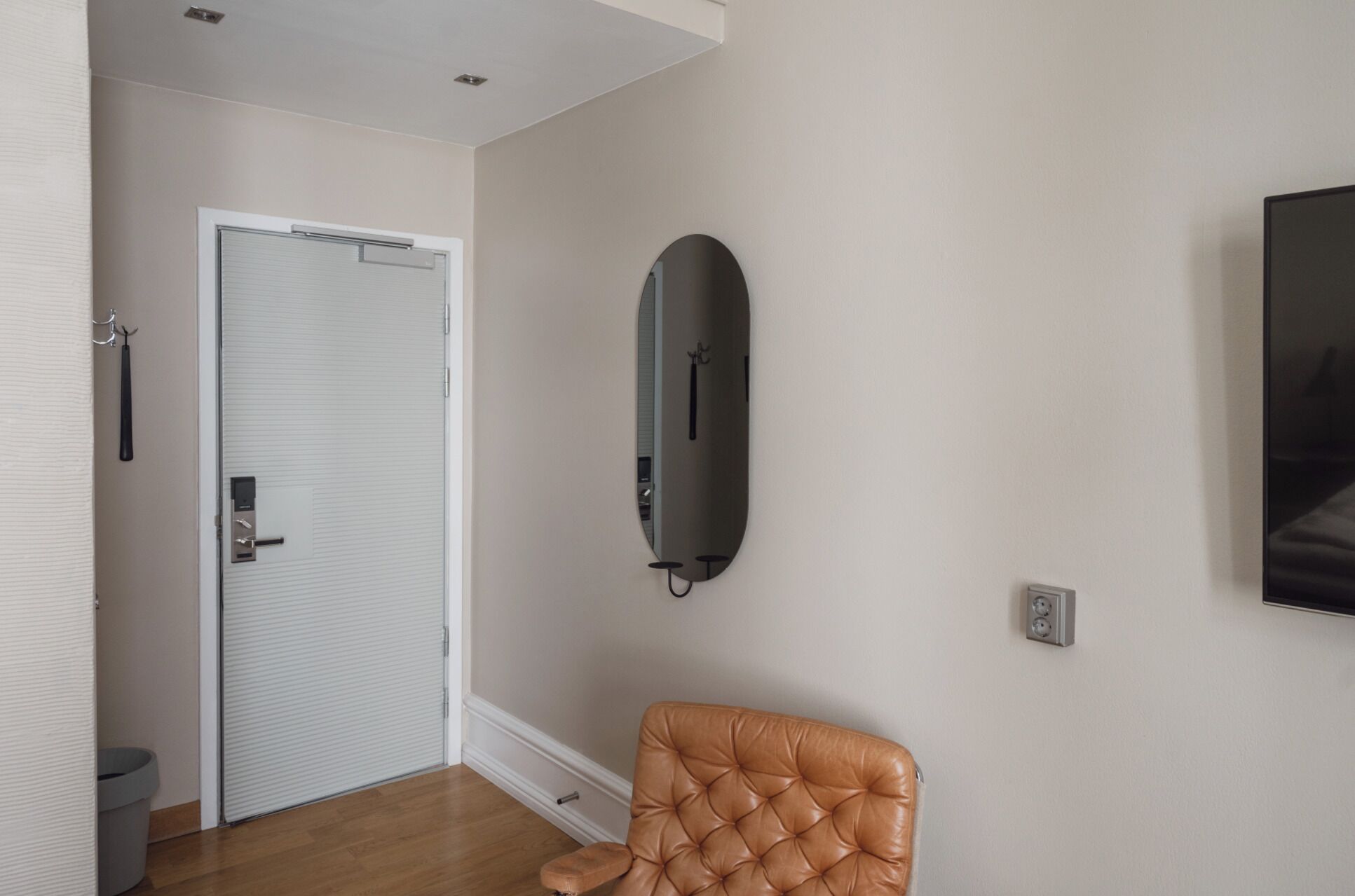 Um quarto com porta fechada, espelho fixado na parede, cadeira e televisão de tela plana.