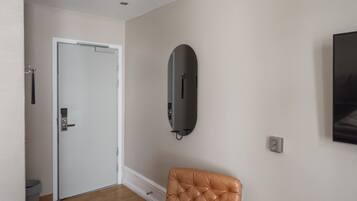 Um quarto com porta fechada, espelho fixado na parede, cadeira e televisão de tela plana.