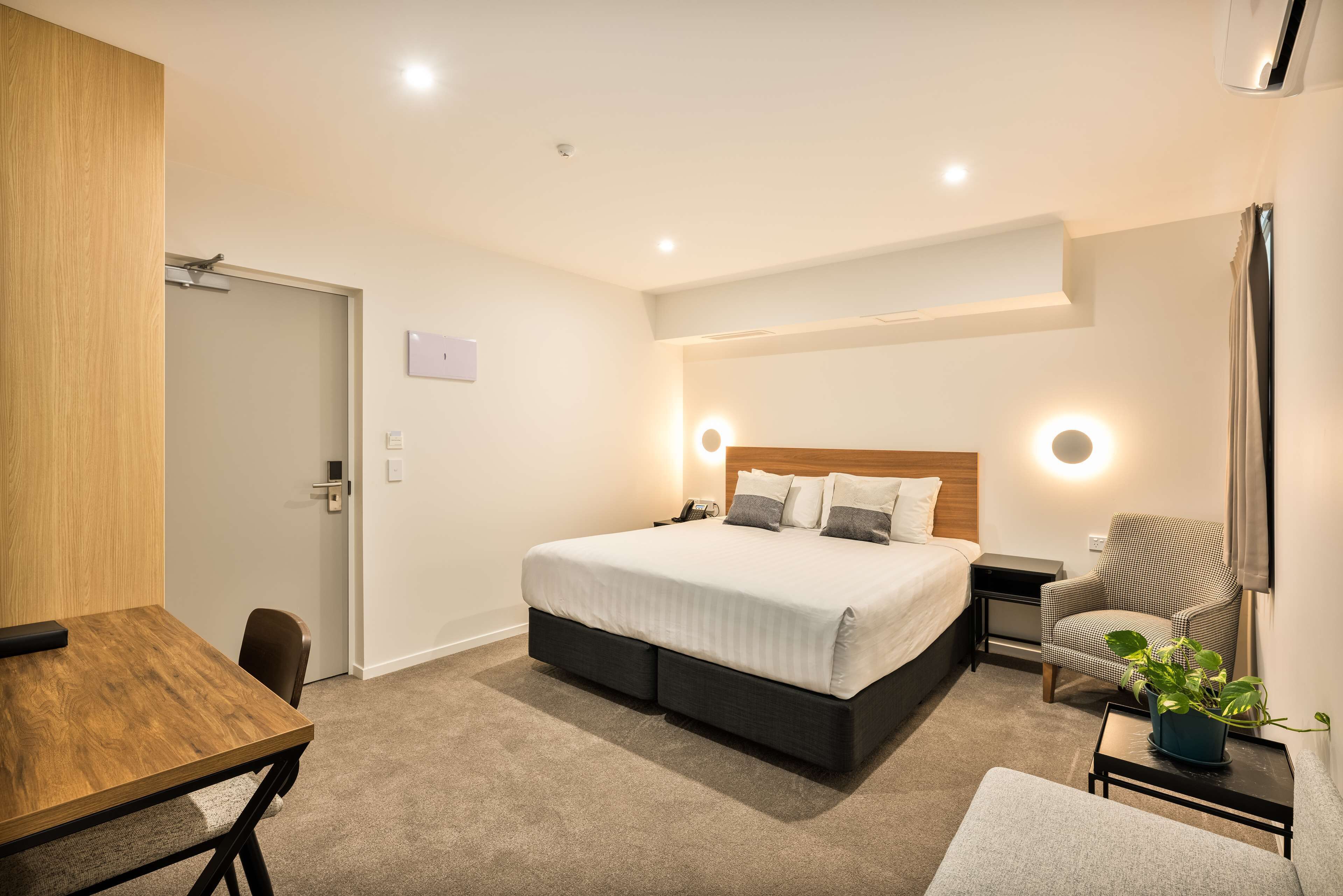 Quarto de hotel moderno com uma cama grande, uma mesa de escritório, uma cadeira e uma pequena mesa com uma planta.
