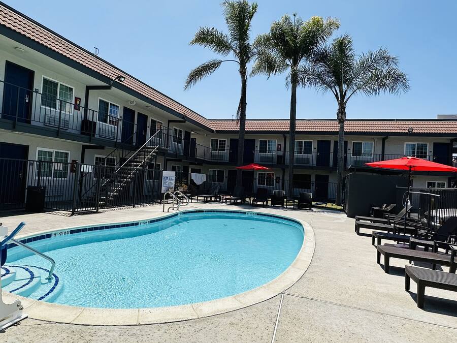 Piscina com espreguiçadeiras e guarda-sóis, cercada por um edifício com varandas e palmeiras.