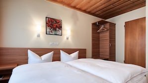 Quarto de hotel com uma cama grande, cabeceira de madeira, duas luminárias fixadas na parede, um quadro, um guarda-roupa e um cabideiro.