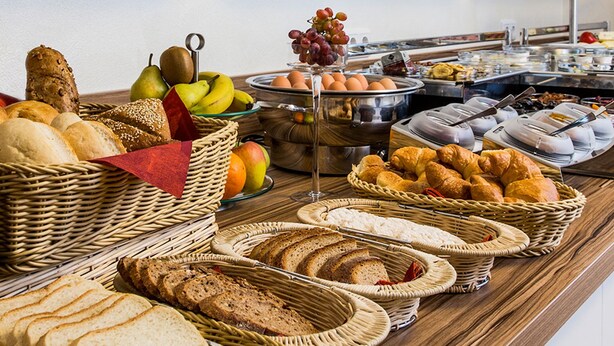 Buffet com diversos pães, frutas e doces.