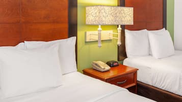 Quarto de hotel com duas camas, mesa de cabeceira com telefone e relógio, e luminária na parede.