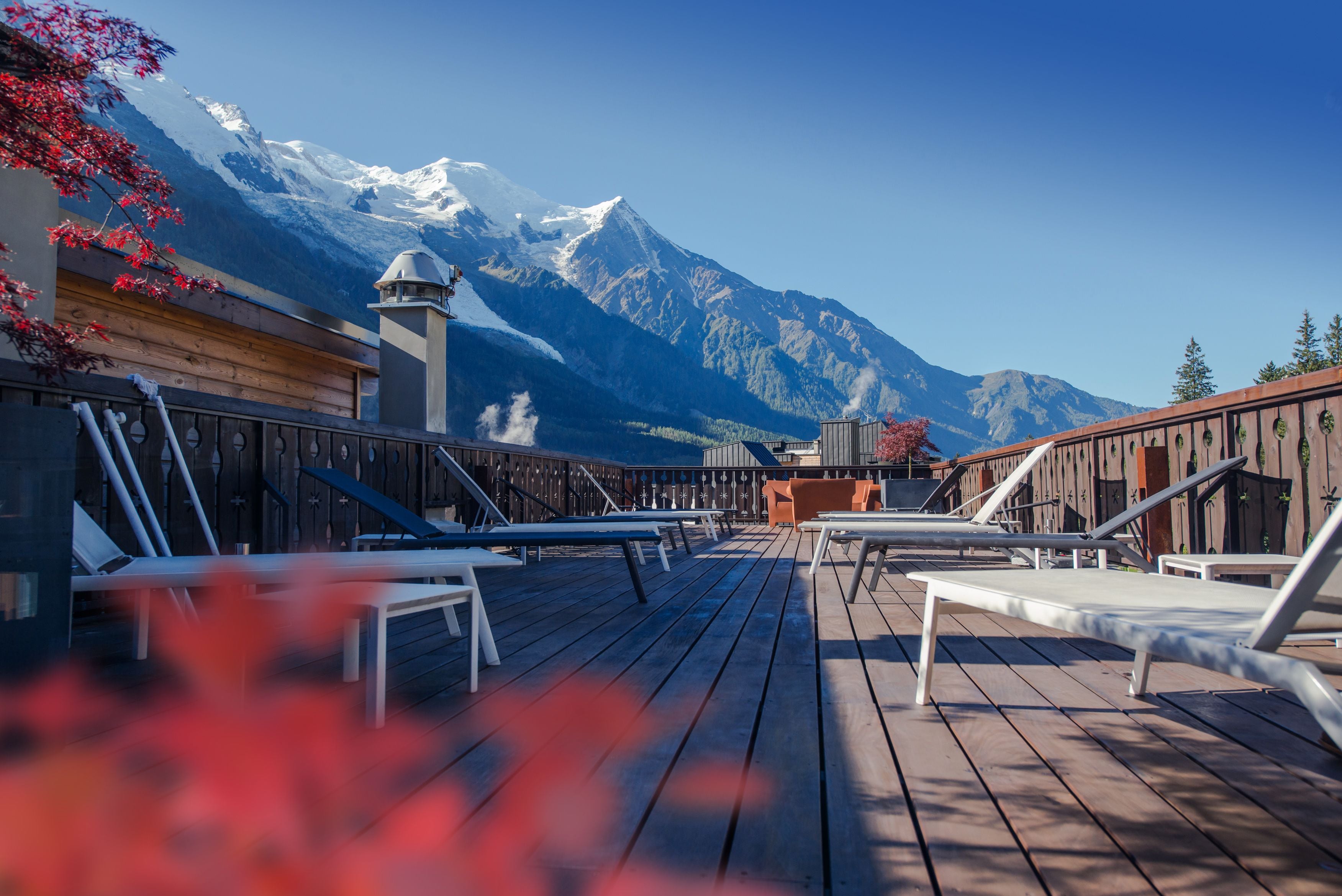 Um deck de madeira com cadeiras de lounge e vista para montanhas nevadas.