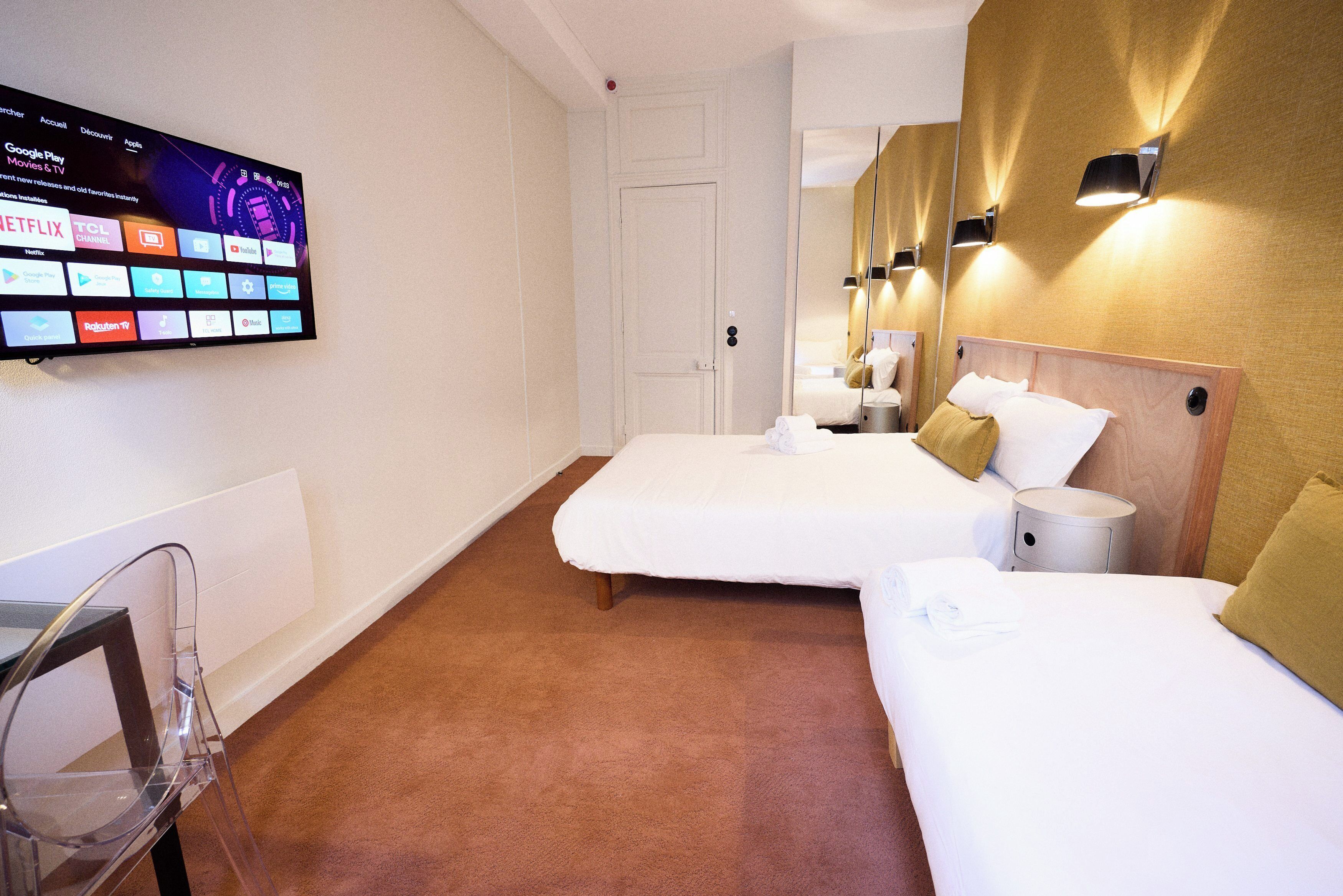 Quarto de hotel com duas camas, uma televisão exibindo serviços de streaming, um espelho e uma mesa de cabeceira.