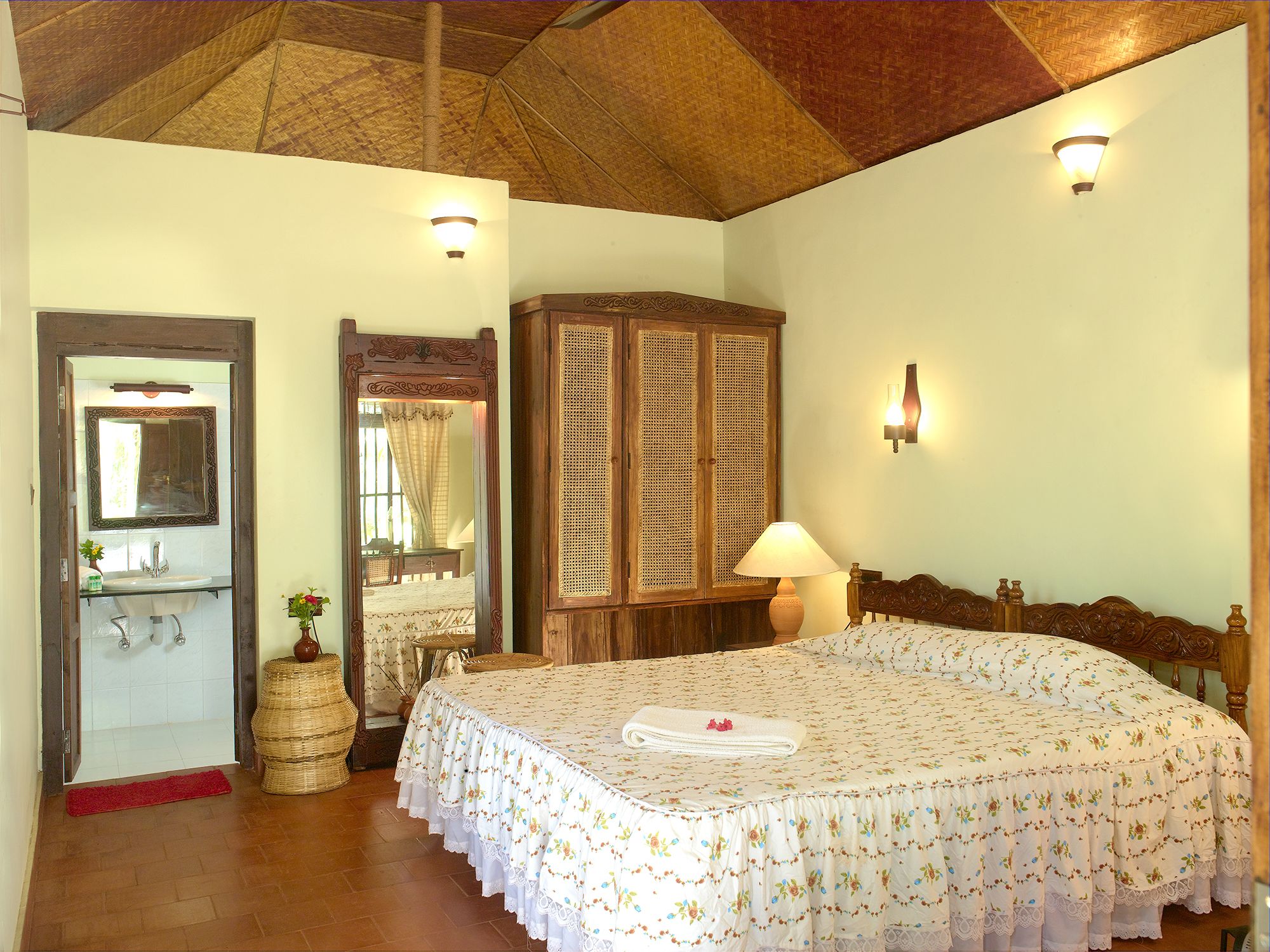 Quarto com cama grande, guarda-roupa de madeira, espelho, mesa de cabeceira com abajur e tapete vermelho na entrada.