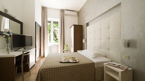 Quarto de hotel com cama, televisão, secretária com um vaso de flores e bandeja de café da manhã sobre a cama.