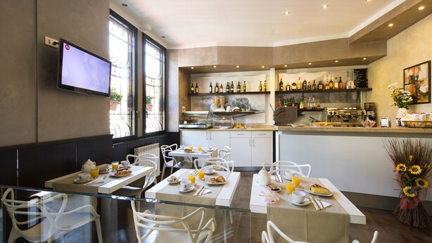 Um restaurante com várias mesas e cadeiras, uma área de cozinha com diversos frascos e equipamentos, e uma televisão fixada na parede.