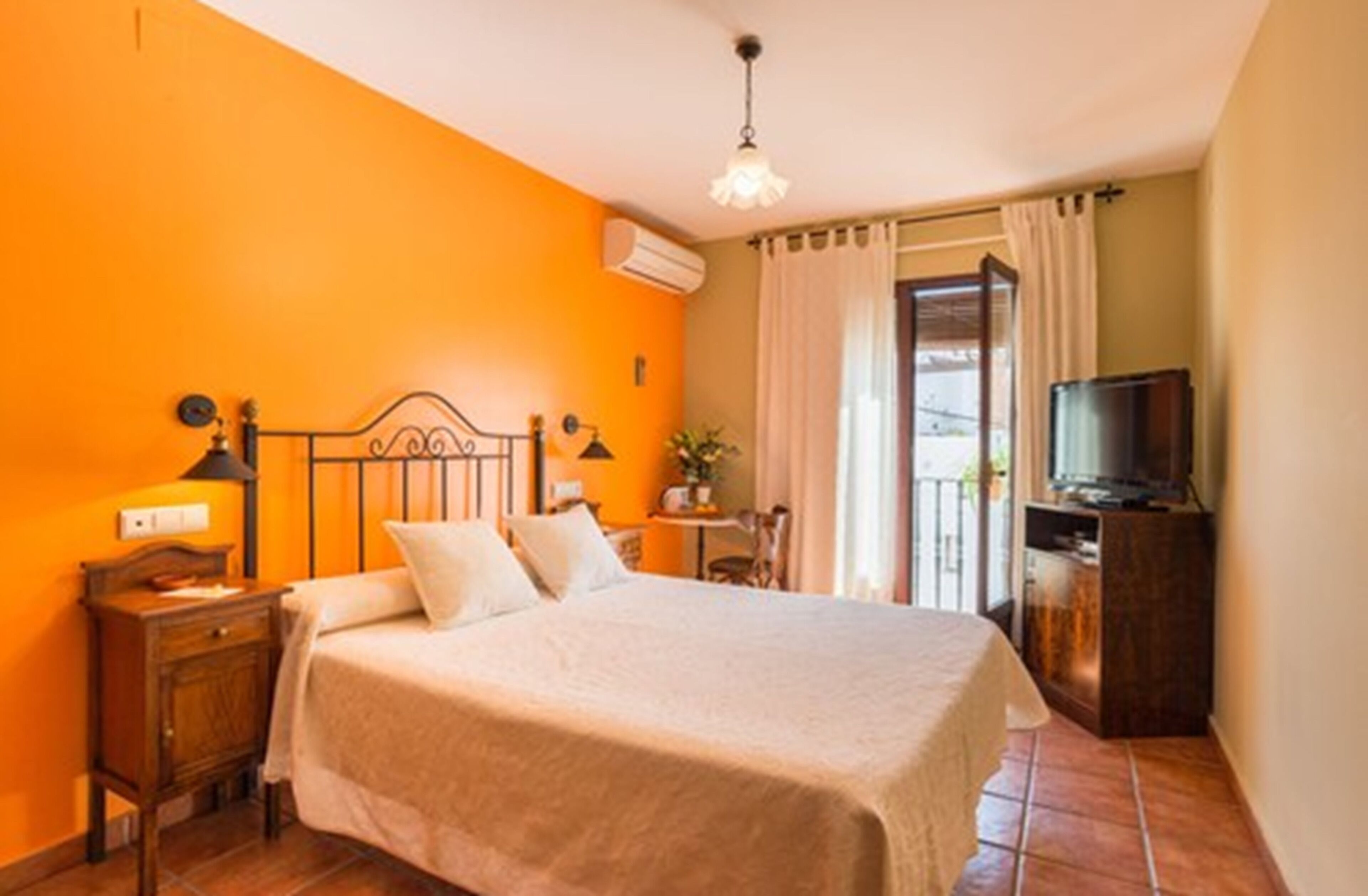Quarto com cama, mesa de cabeceira, luminária, televisão e janela com cortinas.