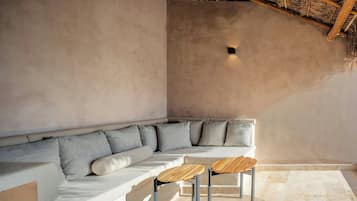 Um interior moderno com um sofá branco curvo, almofadas cinzentas e duas cadeiras de madeira.