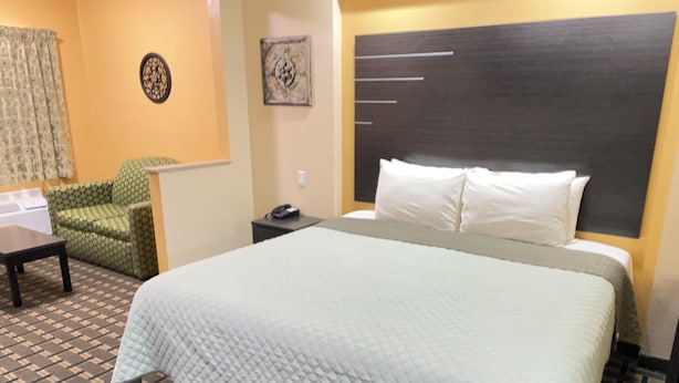 Quarto de hotel com cama, uma cadeira, mesa de cabeceira e uma parede com obras de arte.