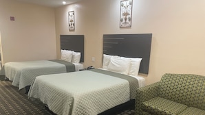 Quarto de hotel com duas camas, um sofá verde estampado e uma mesinha.