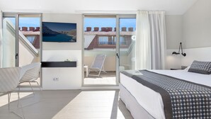 Quarto de hotel com cama, poltrona, televisão e varanda com vista para prédios.