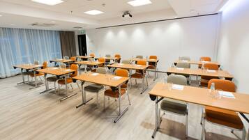 Uma sala de conferências com várias mesas e cadeiras, um projetor e um quadro branco.